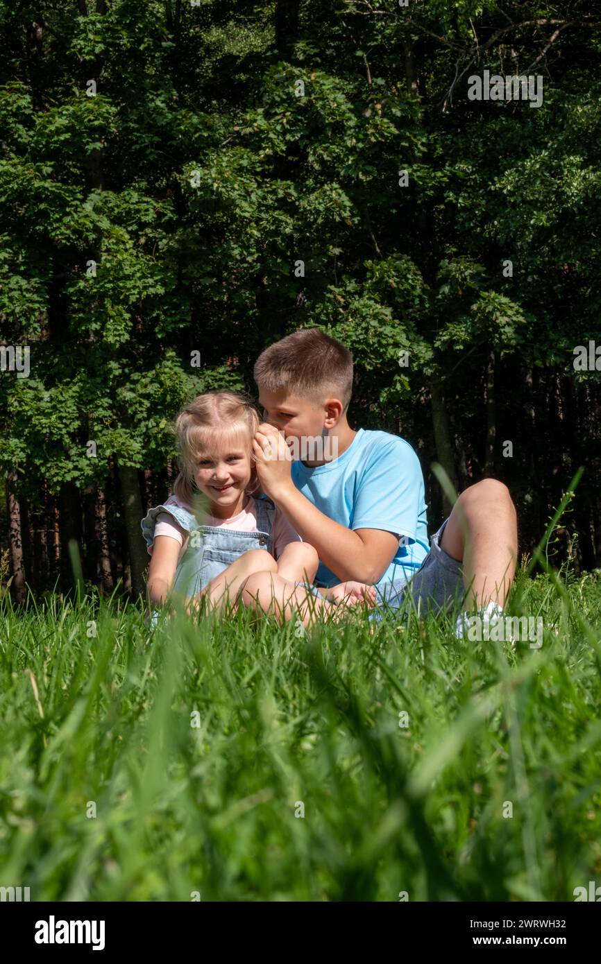 The boy in casual attire leans close, whispering to the girl in denim ...