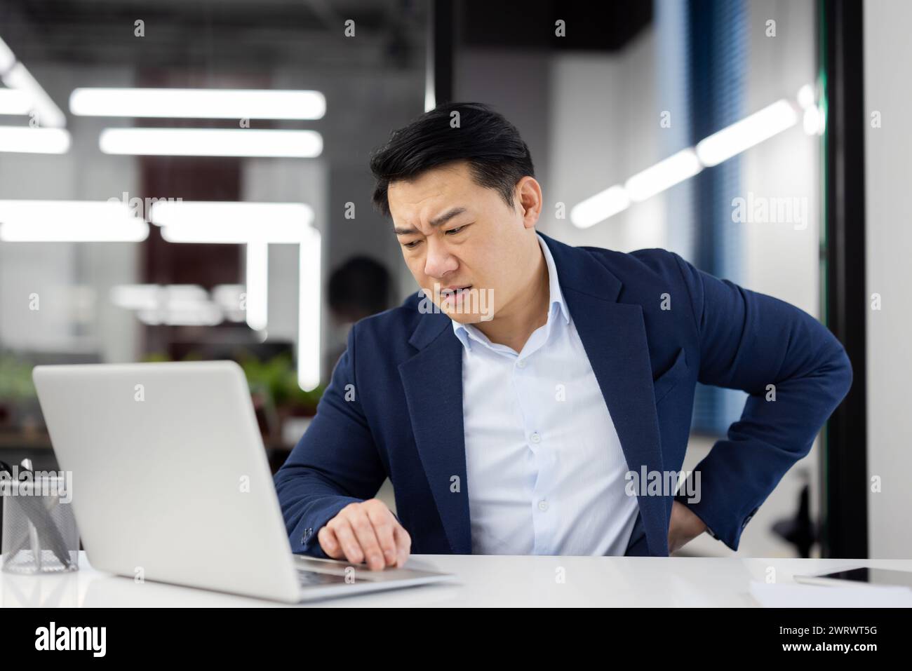 Worried Asian young man sitting in office at desk in front of laptop ...