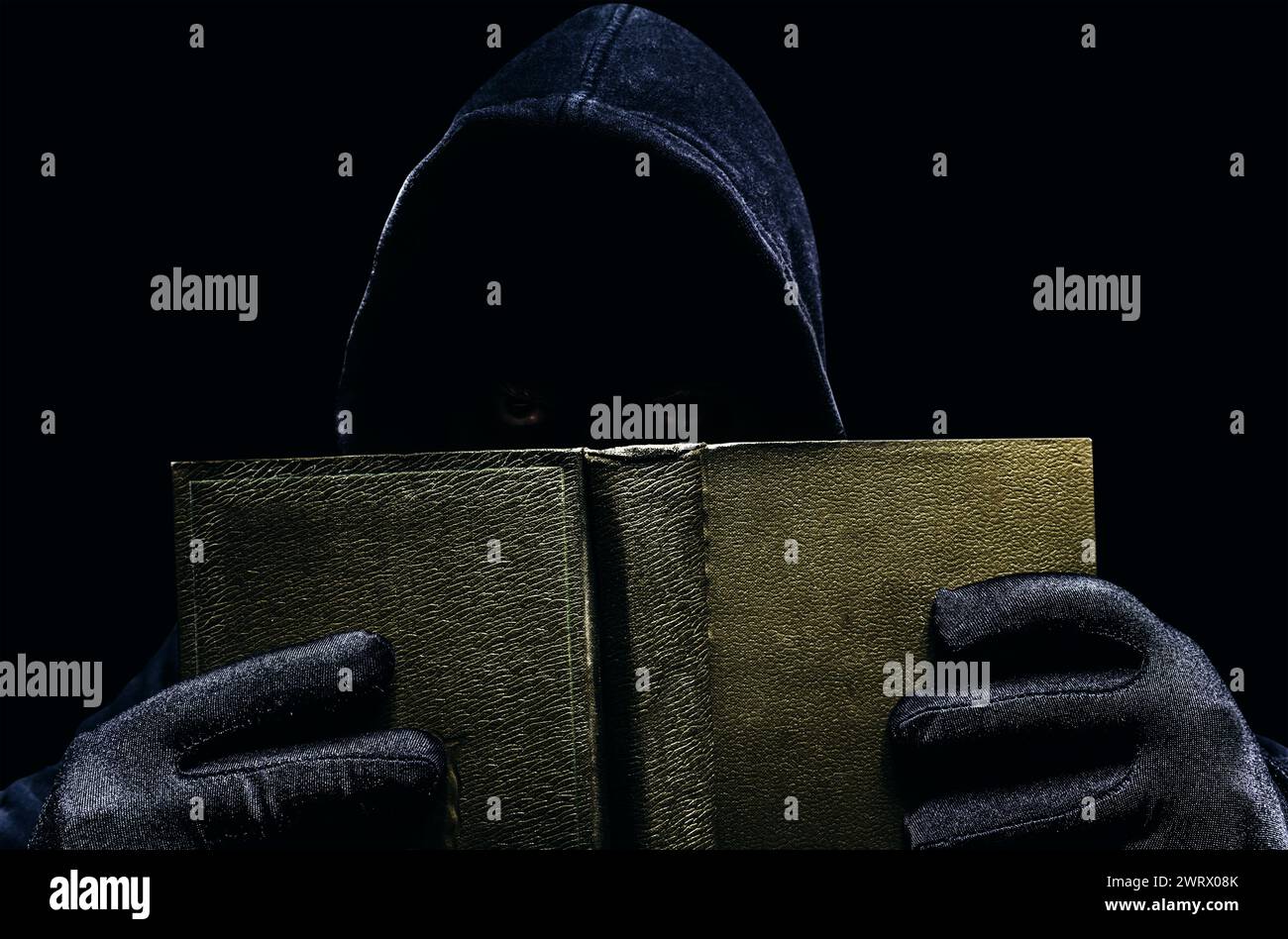 Photo of scary shaded hooded man holding opened book and peaking on ...