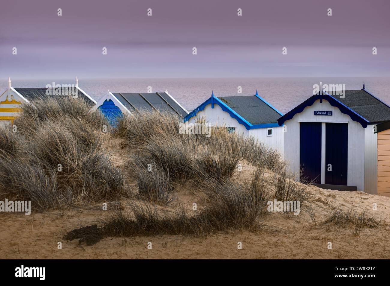 Row of colourful wooden beach huts with sand dune and beach grasses in ...