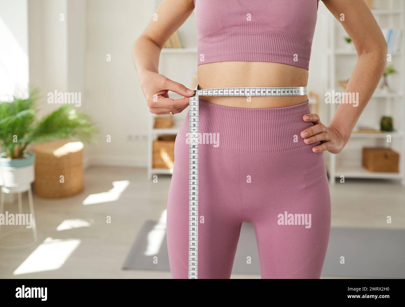 Woman with beautiful perfect fit body measures her thin waist with ...