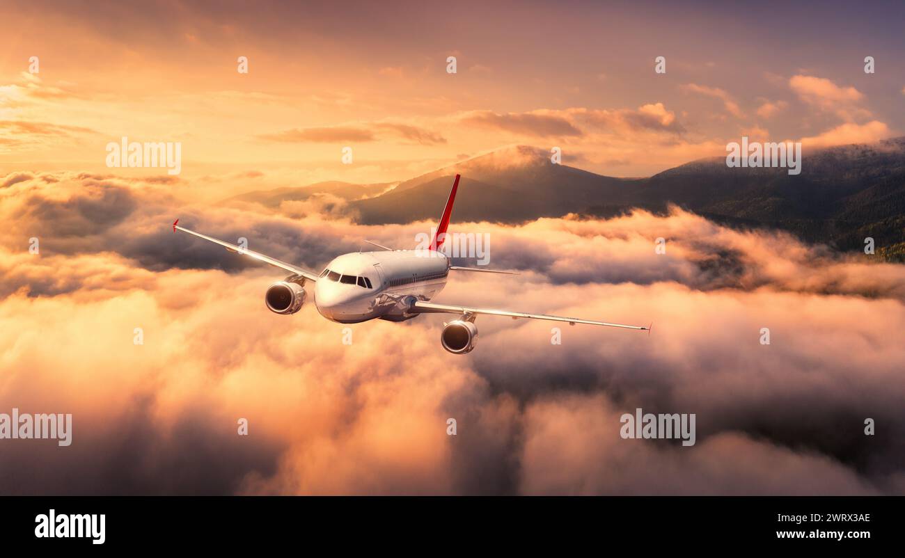 Plane is flying over mountains in low clouds at golden sunrise Stock ...