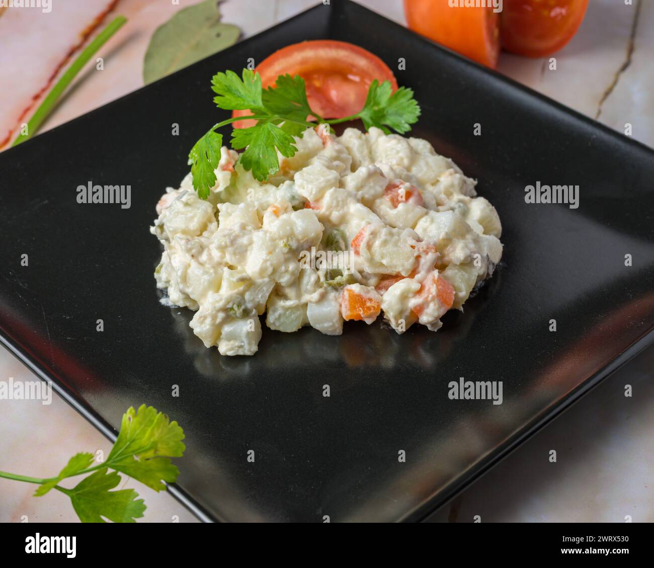 Russian salad Creamy potato salad garnished with parsley on a black ...
