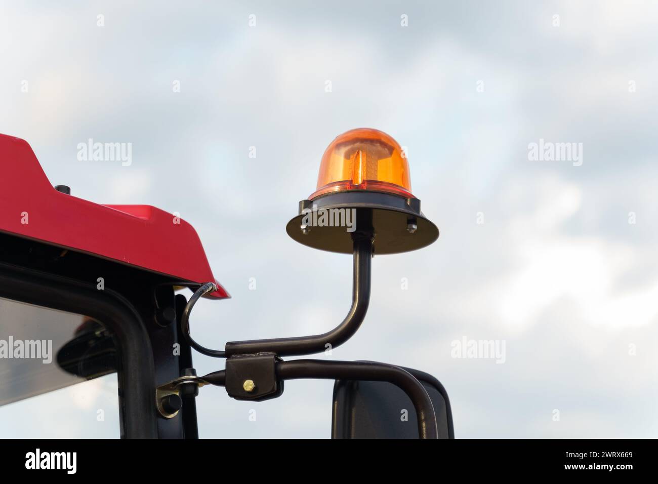 Orange warning beacon light mounted on the cab of a red farm tractor ...