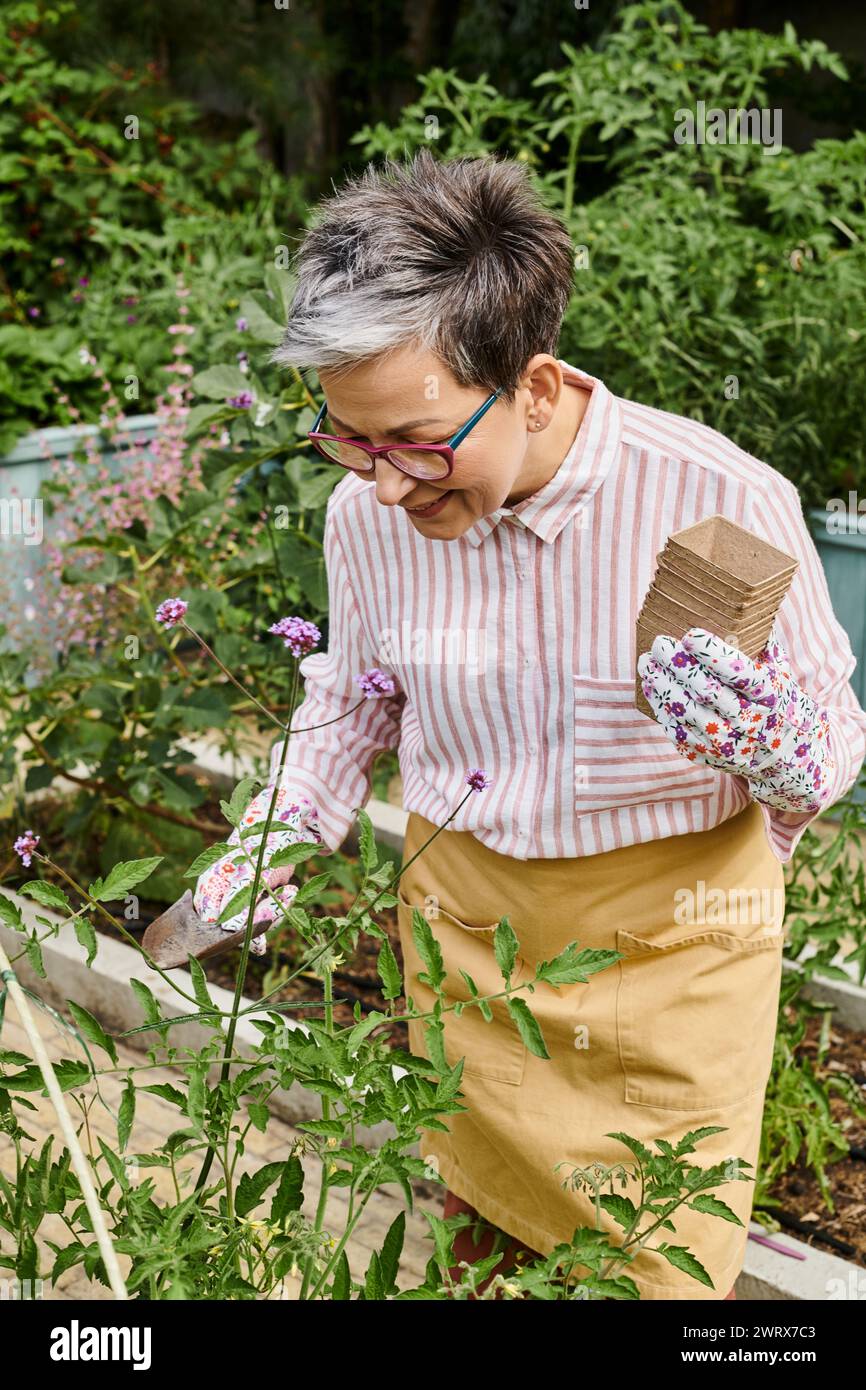 attractive jolly mature woman with glasses and gloves using gardening ...