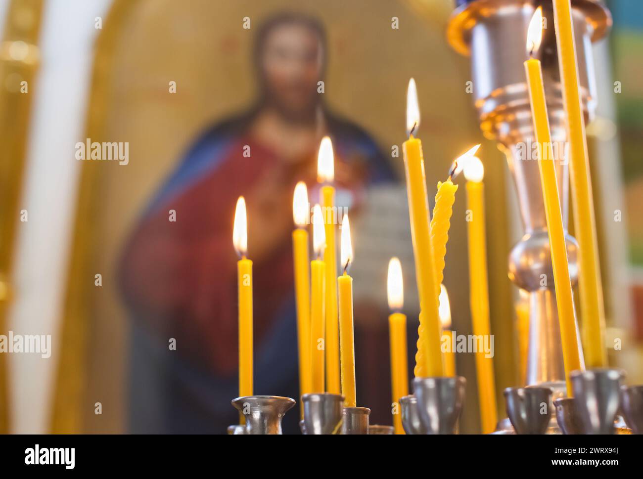 Church candles burn in the church against the background of the icon of ...
