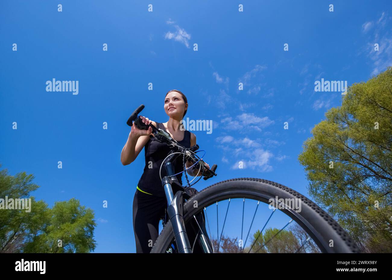 Girl athlete in black tracksuit rides a bike in the morning in the park ...