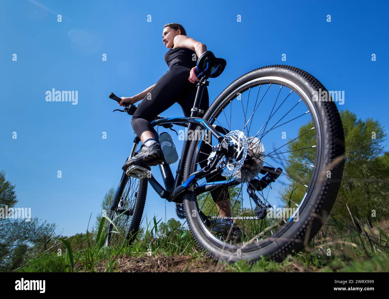 Girl athlete in black tracksuit rides a bike in the morning in the park ...