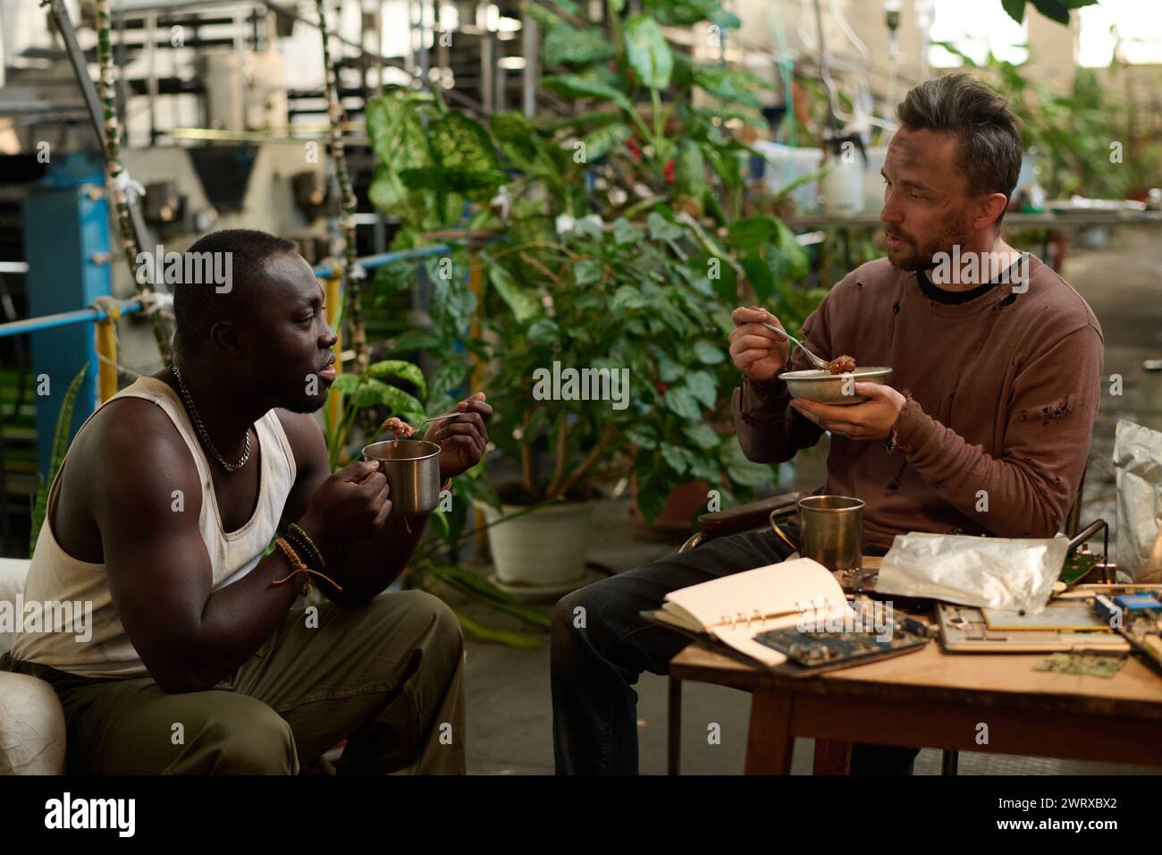 Two ethnically diverse men wearing shabby clothes having lunch and ...