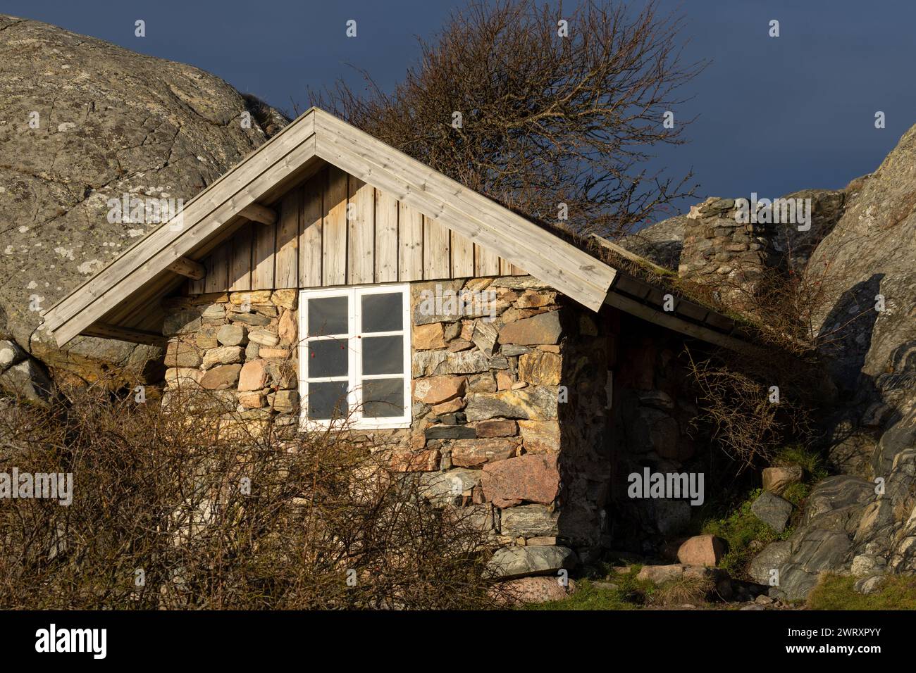 Stone cottage with window in sunlight surrounded by cliffs and ...