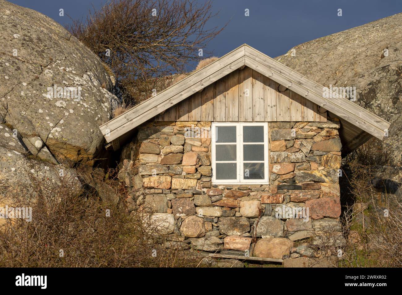 Stone cottage with window in sunlight surrounded by cliffs and ...