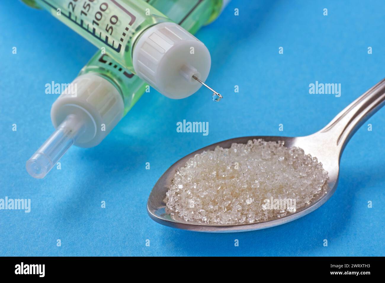 Insulin syringes with a drop of insulin above a spoon of white sugar ...