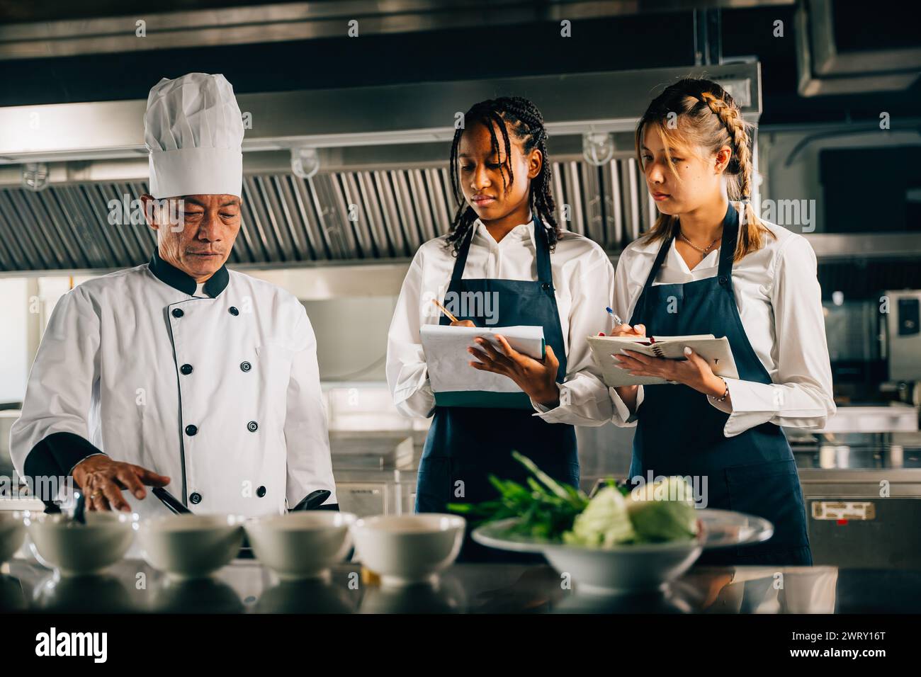 Professional Asian senior chef teaching cooking techniques to diverse ...