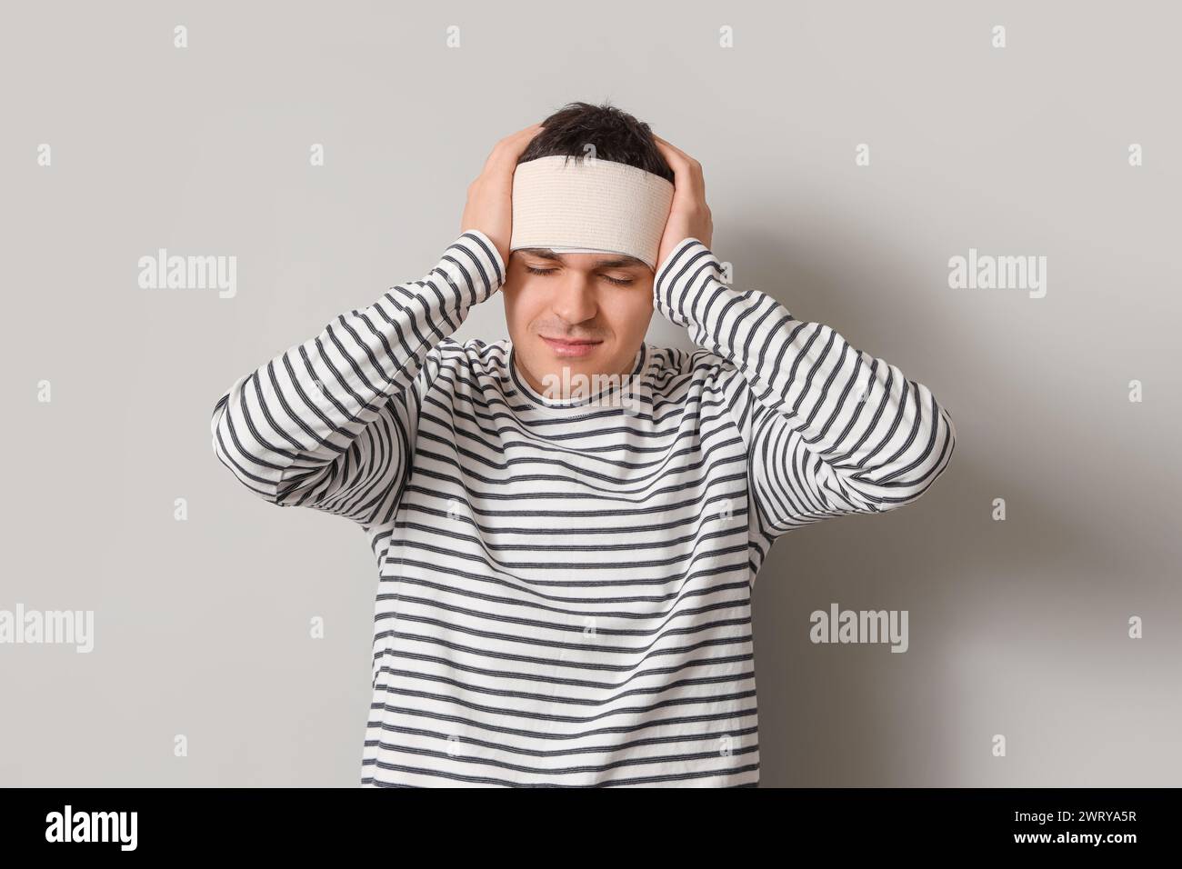Young man with brain concussion and bandaged head on light background ...