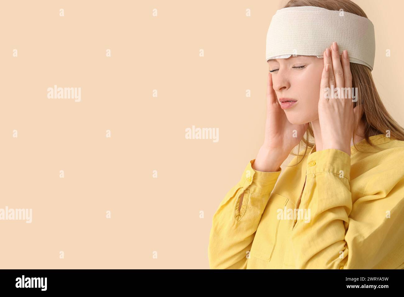Young woman with brain concussion and bandaged head on beige background ...