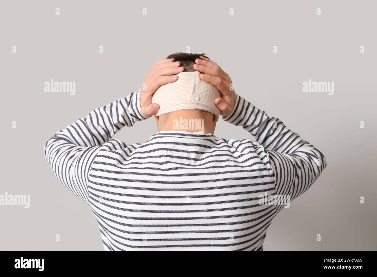 Young man with brain concussion and bandaged head on light background ...