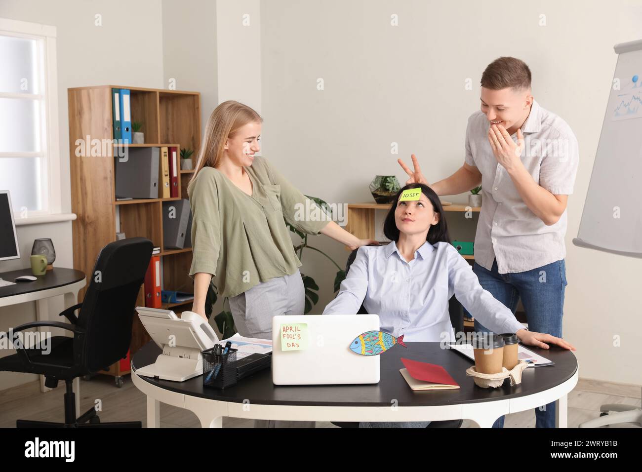 Young woman with sticky paper on her forehead and laughing colleagues ...
