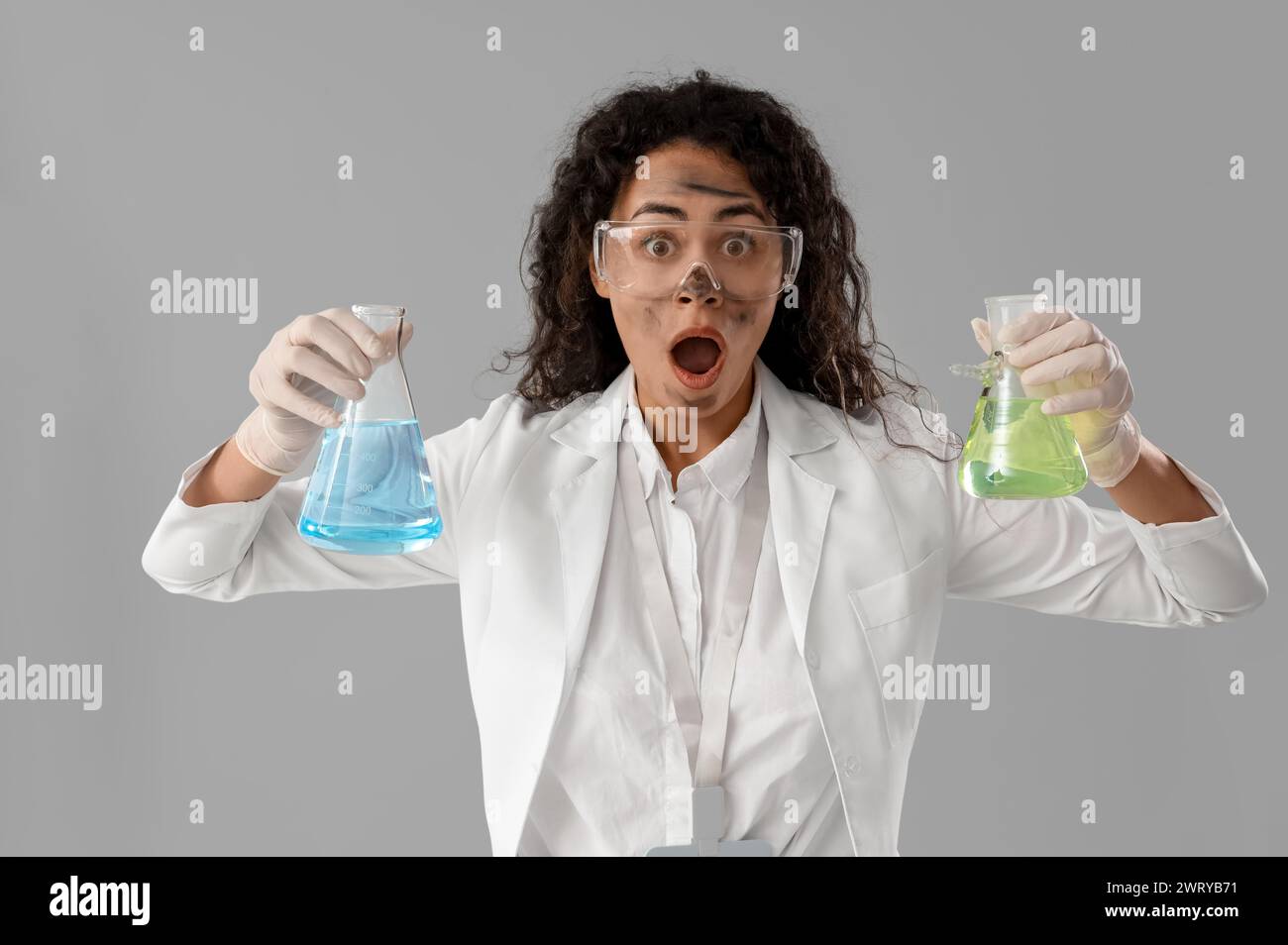 Shocked female African-American chemist with flasks on light background ...