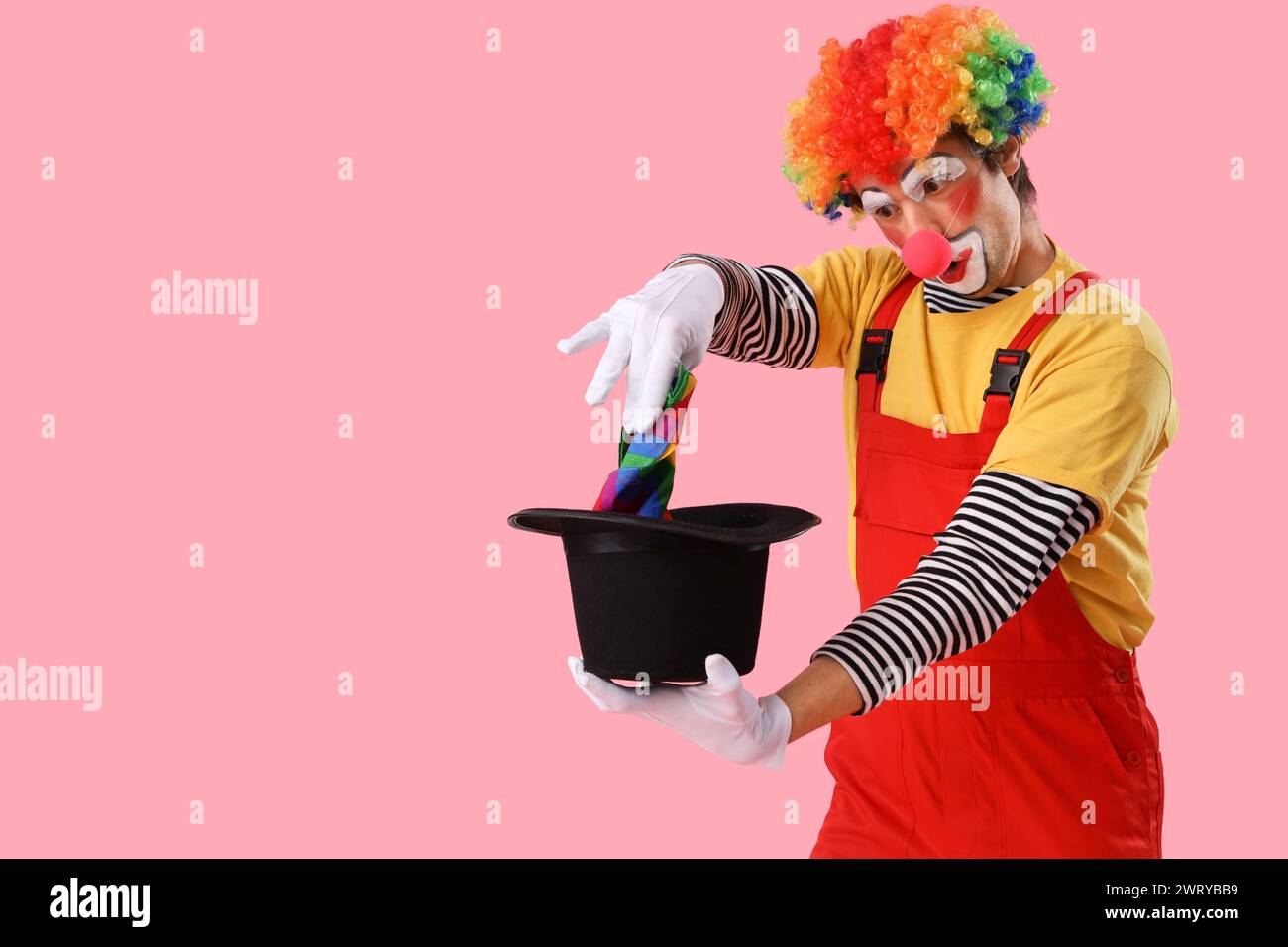 Portrait of clown showing magic trick on pink background. April Fool's ...