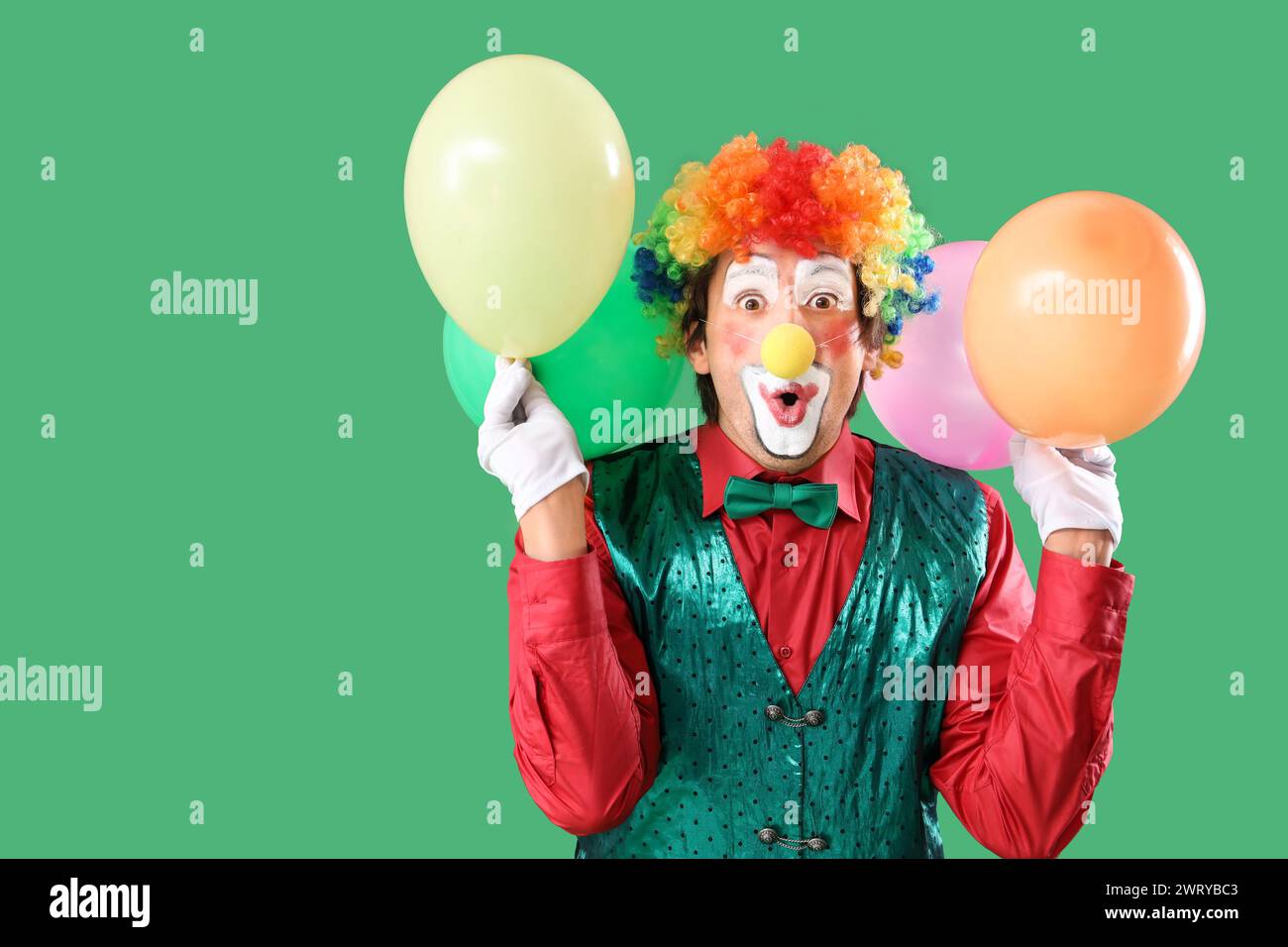 Portrait of surprised clown with balloons on green background. April ...