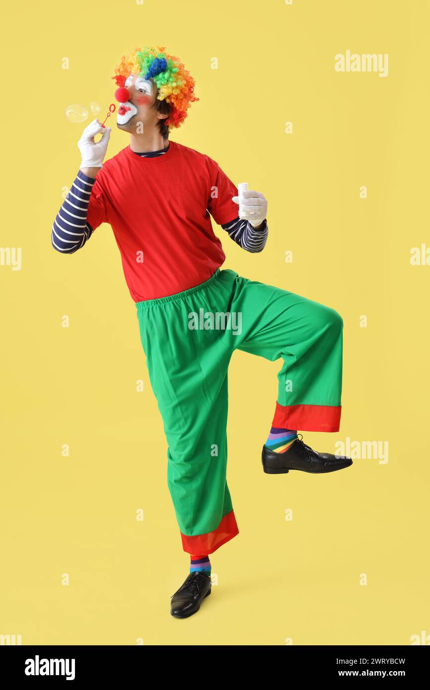 Portrait of clown blowing soap bubbles on yellow background. April Fool ...