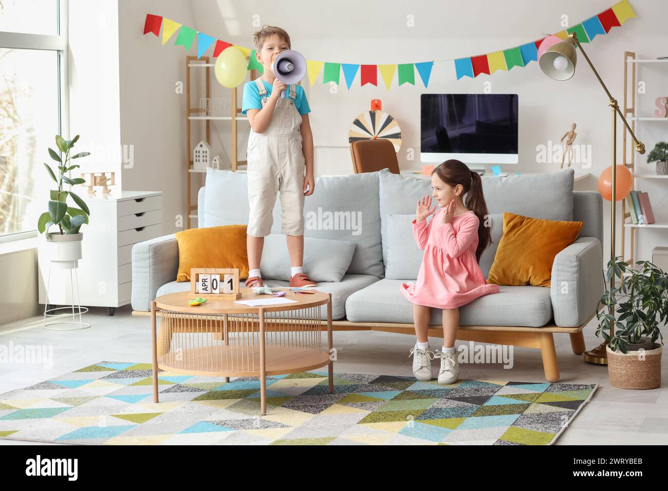 Cute little boy scaring his sister with megaphone at home. April Fool's ...