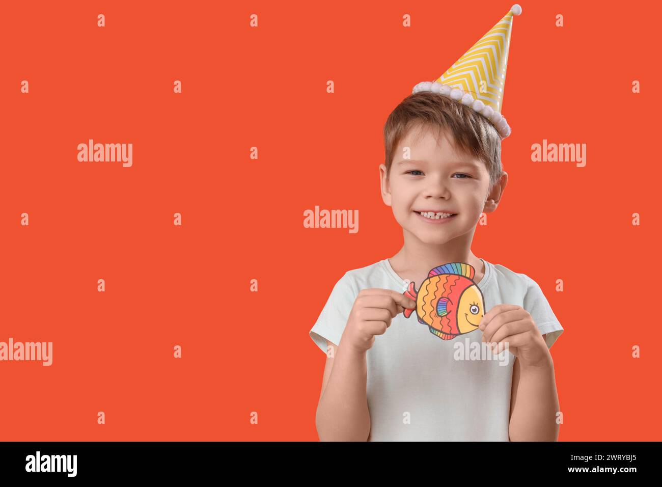 Cute little boy with party hat and paper fish on orange background ...