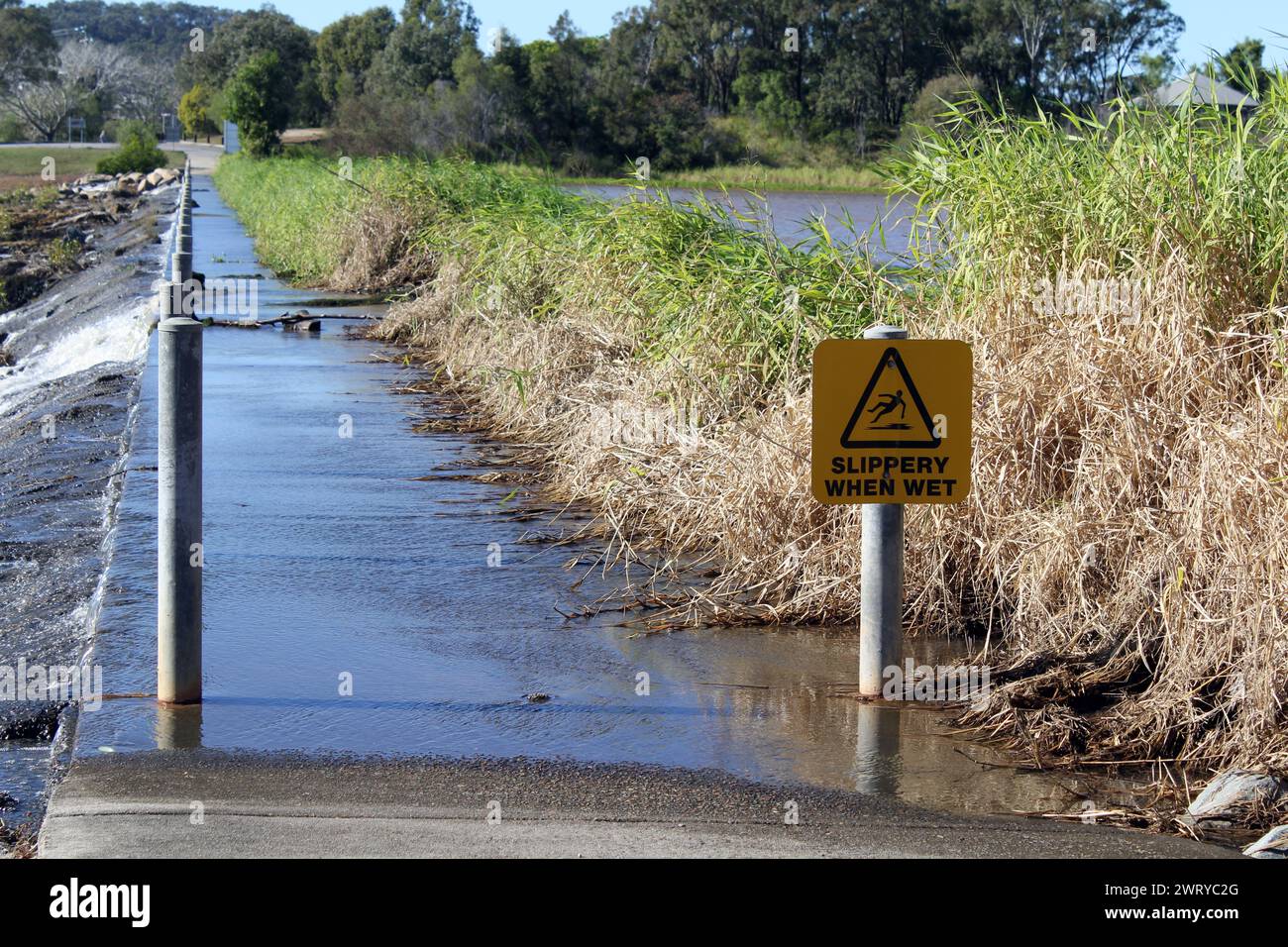 Causeway over a lake with a slippery when wet sign Stock Photo - Alamy
