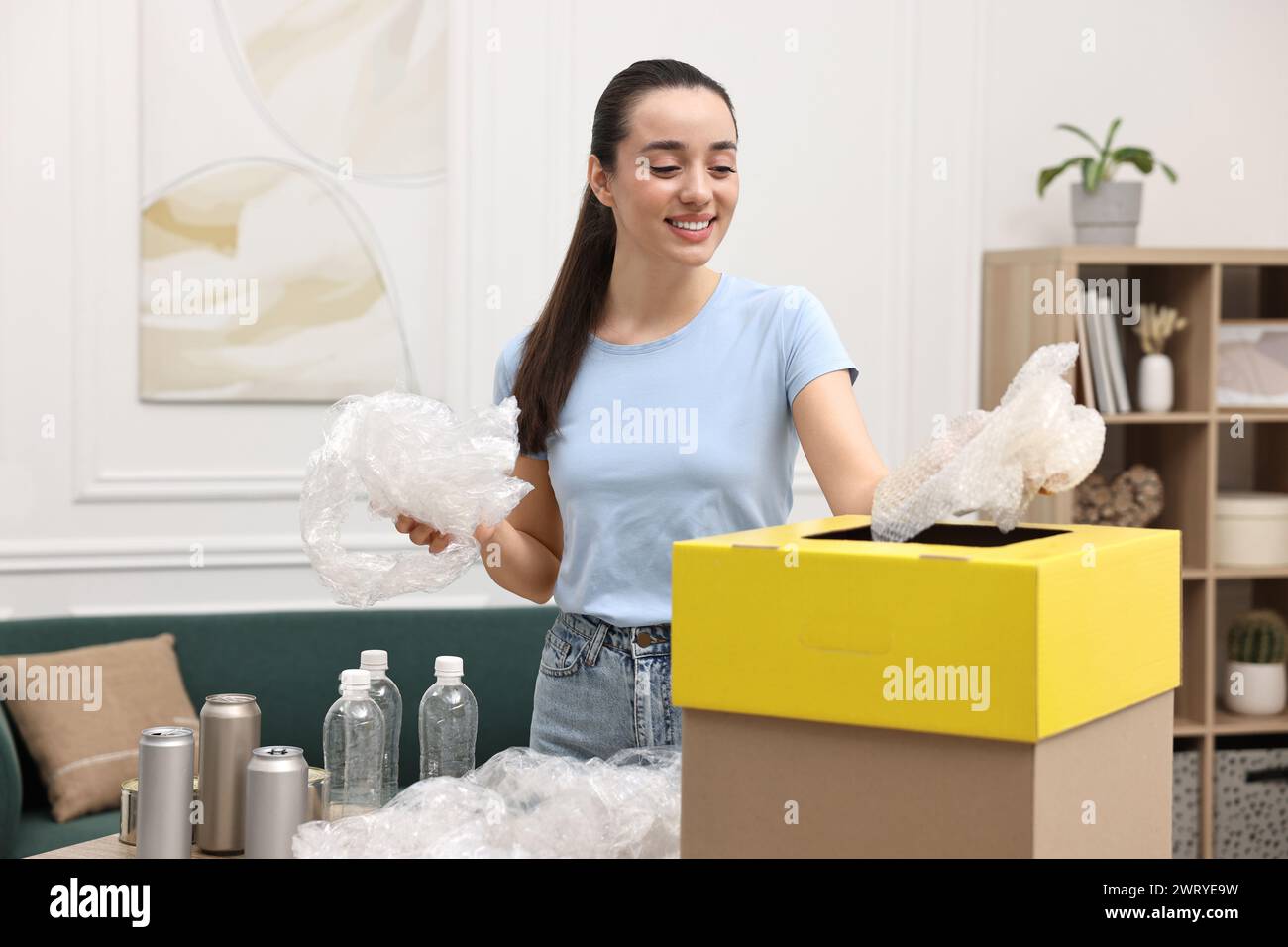 Garbage sorting. Smiling woman throwing plastic package into cardboard ...