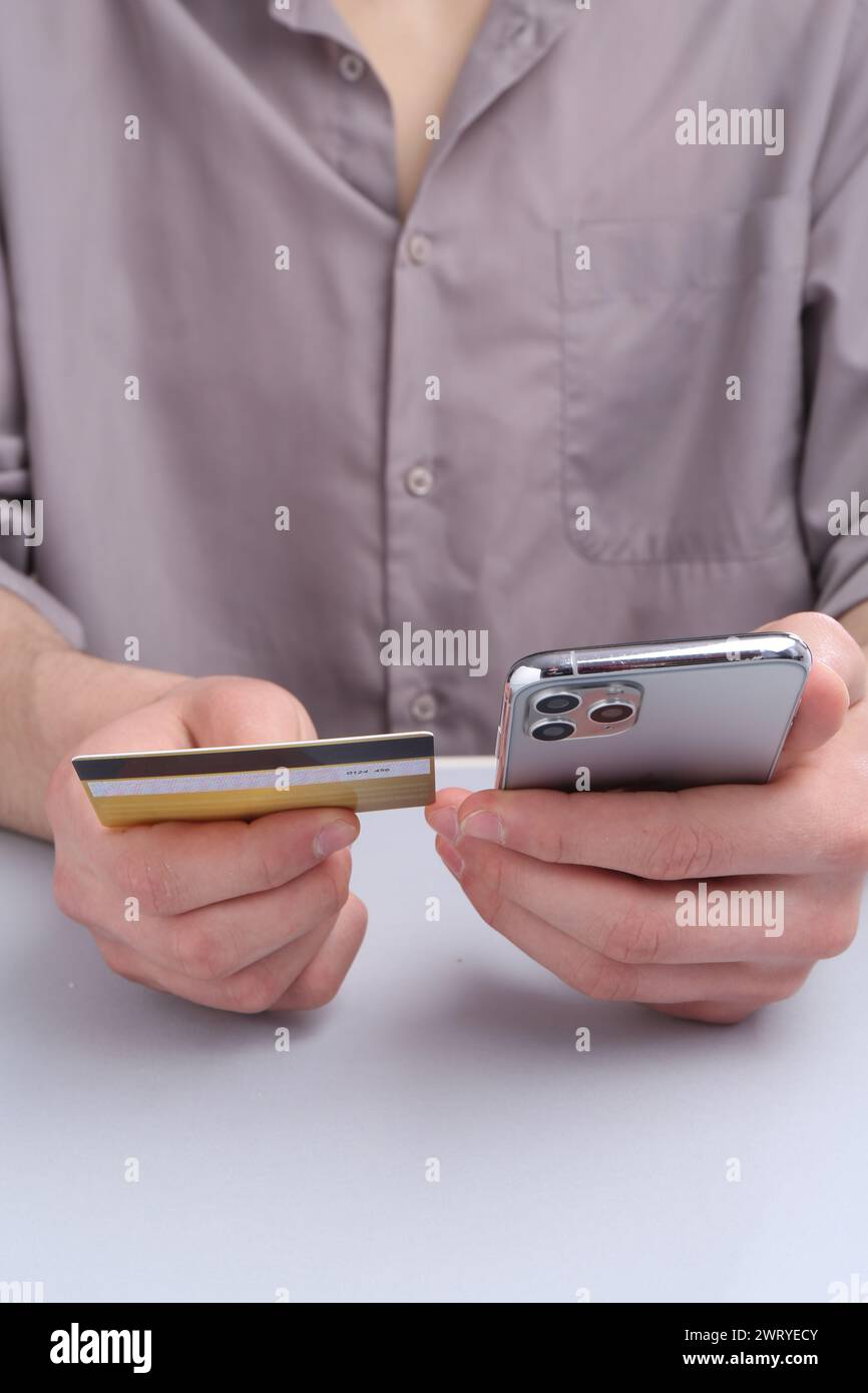 Online payment. Man with smartphone and credit card at light grey table ...