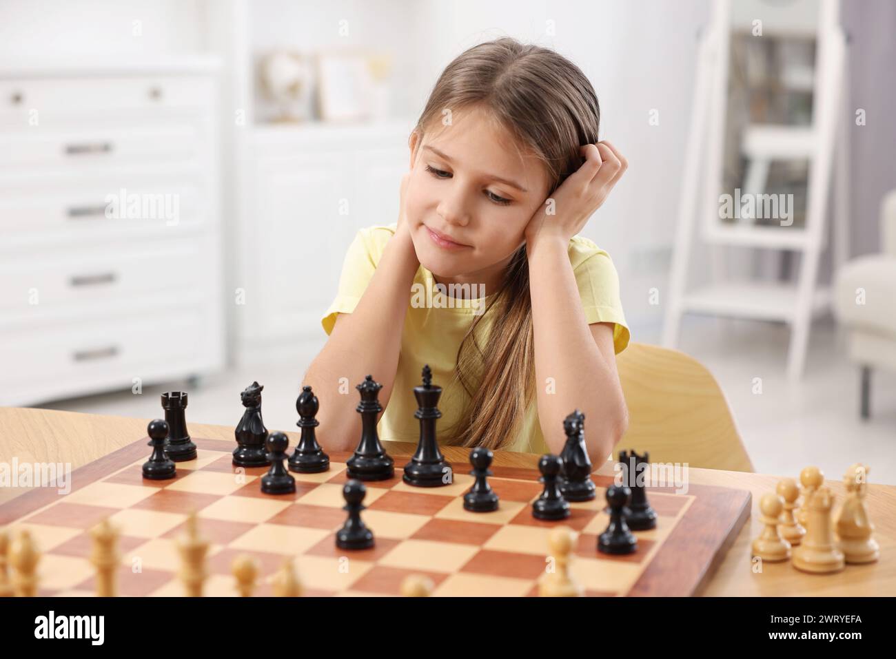 Cute girl playing chess at table in room Stock Photo - Alamy
