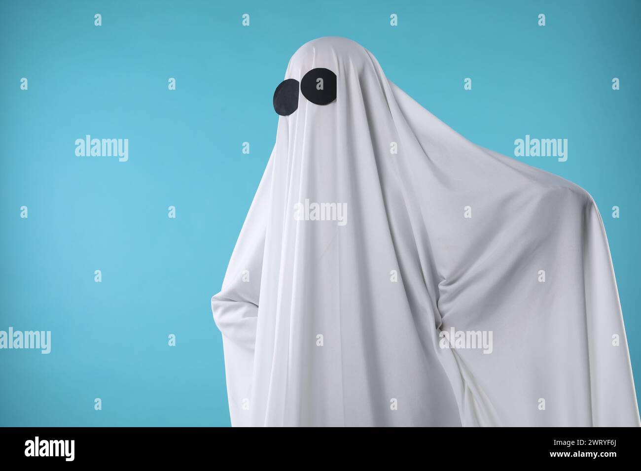 Creepy ghost. Person covered with white sheet on light blue background ...