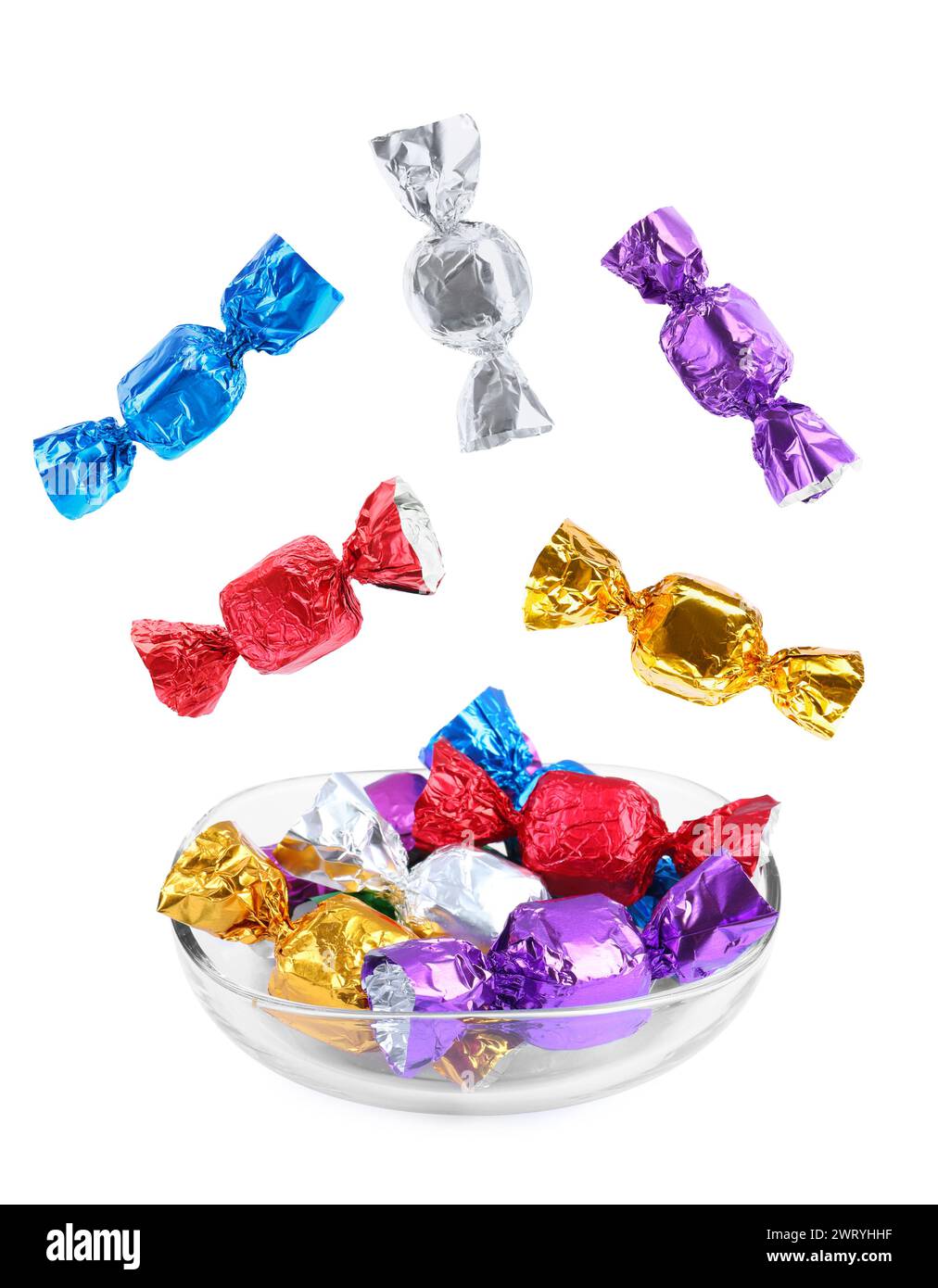 Tasty candies in bright wrappers falling into glass bowl on white ...