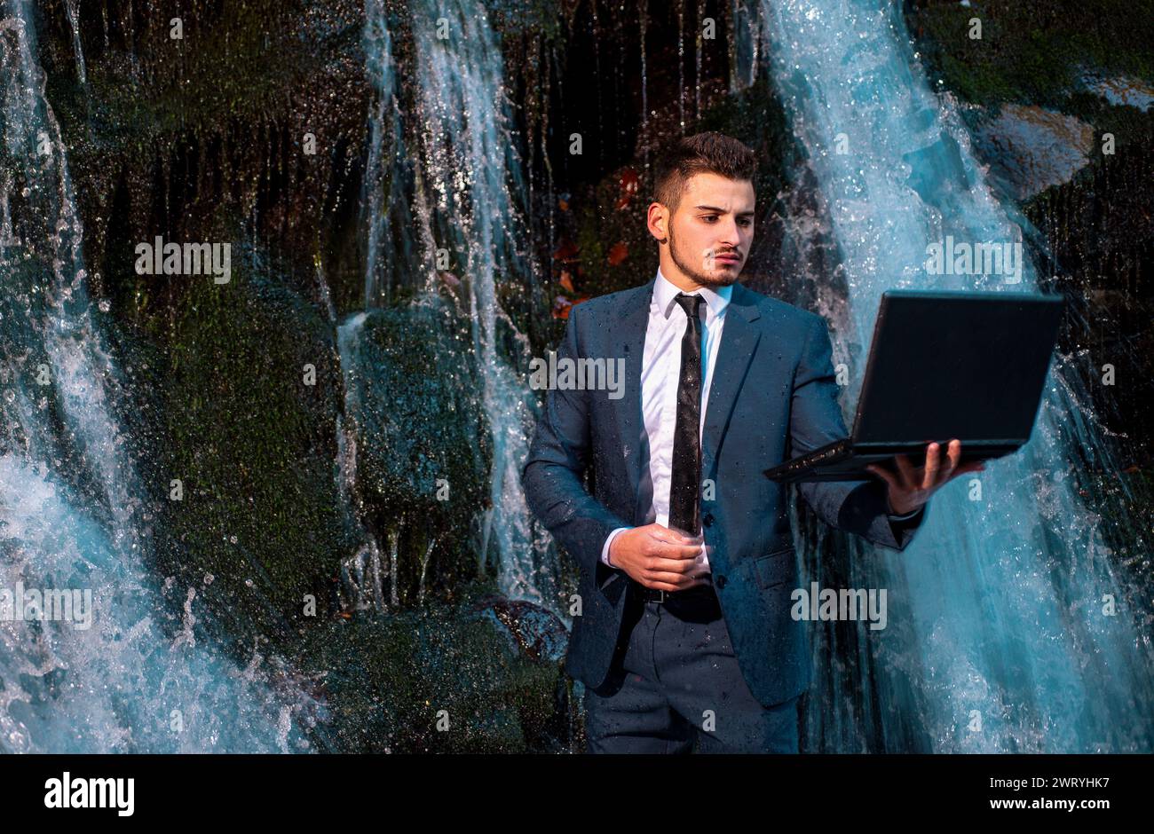 Attractive business man in suit holding laptop at waterfall background ...