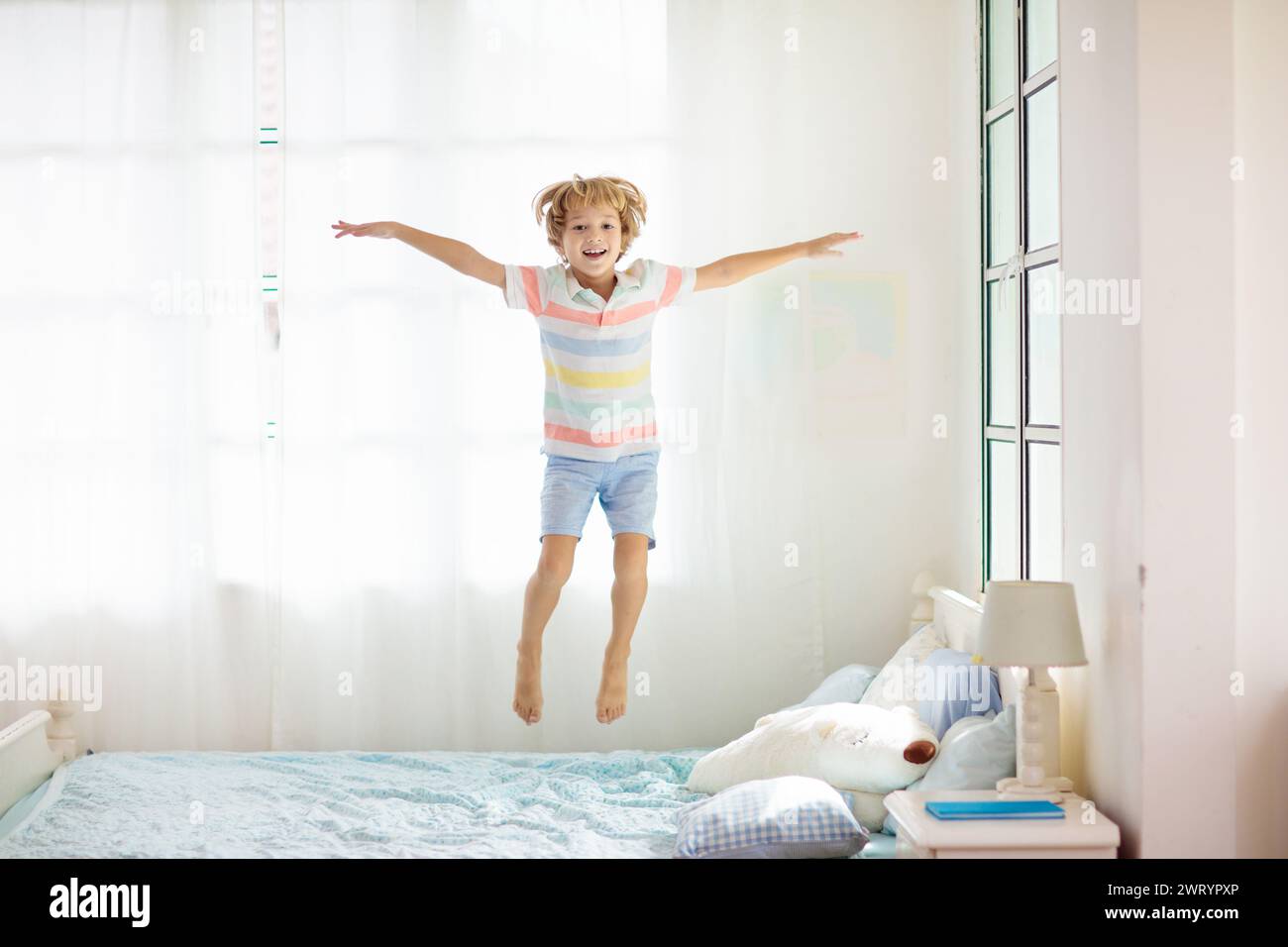 Child jumping on bed in white bedroom with big window. Kids play at ...