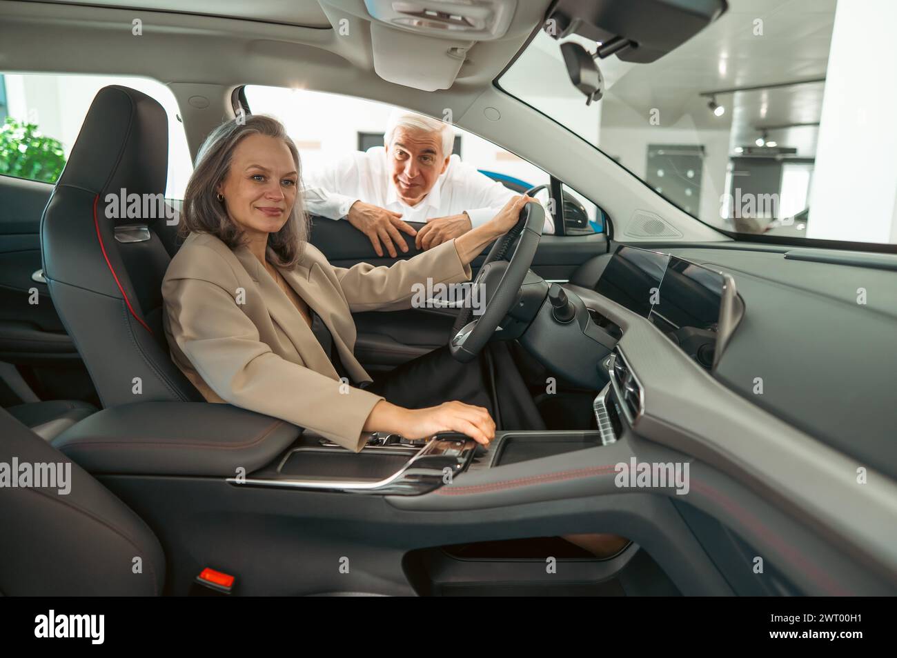 An elderly couple chooses a new car at a car dealership. Mature woman ...