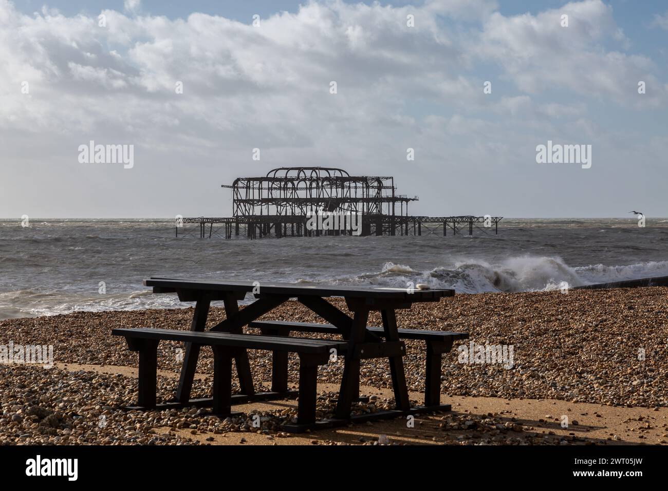 A picnic table and bench on the beach at Brighton, with the ruins of ...