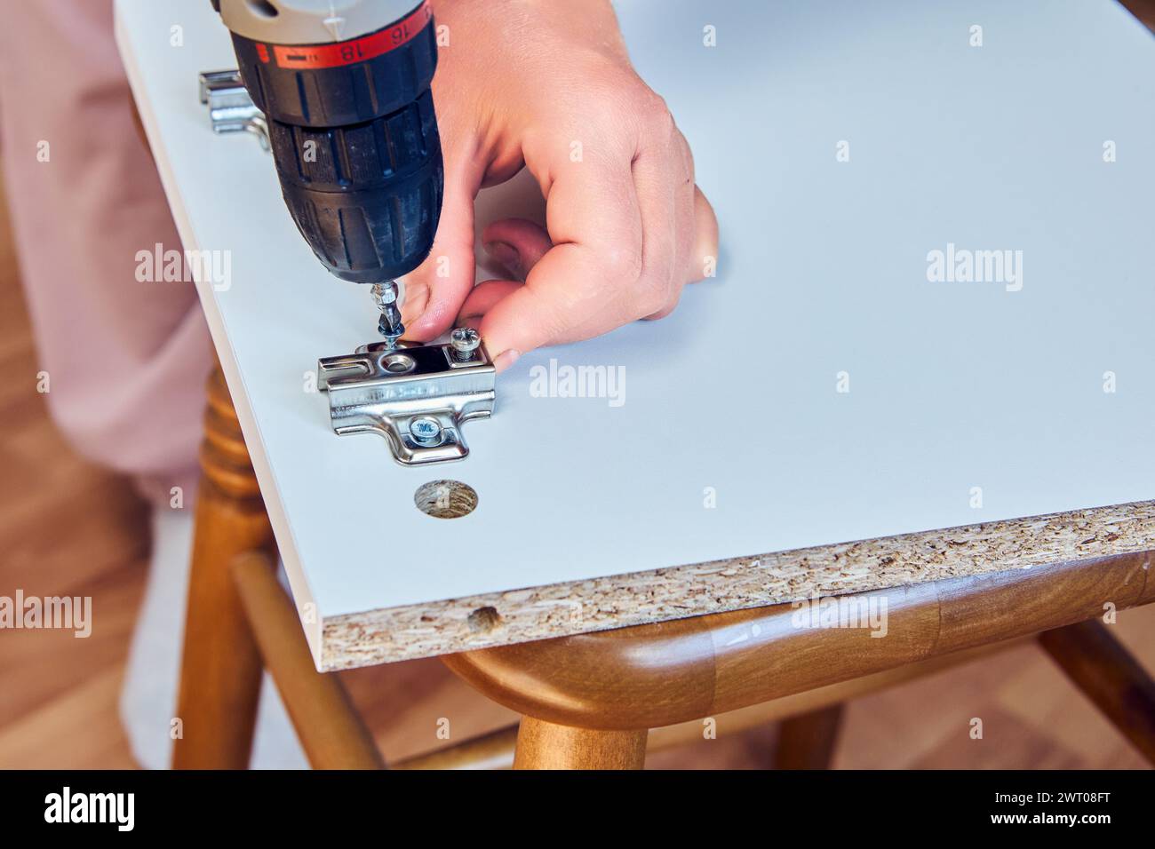 Furniture assembler installs adjustable door hinges into particle board ...