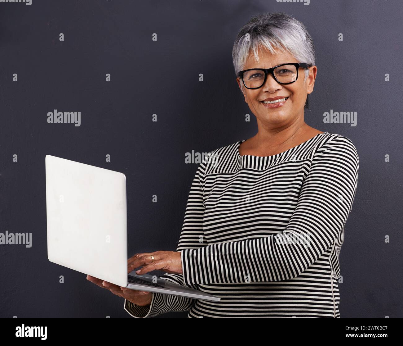 Laptop, typing and portrait of mature woman in studio background ...