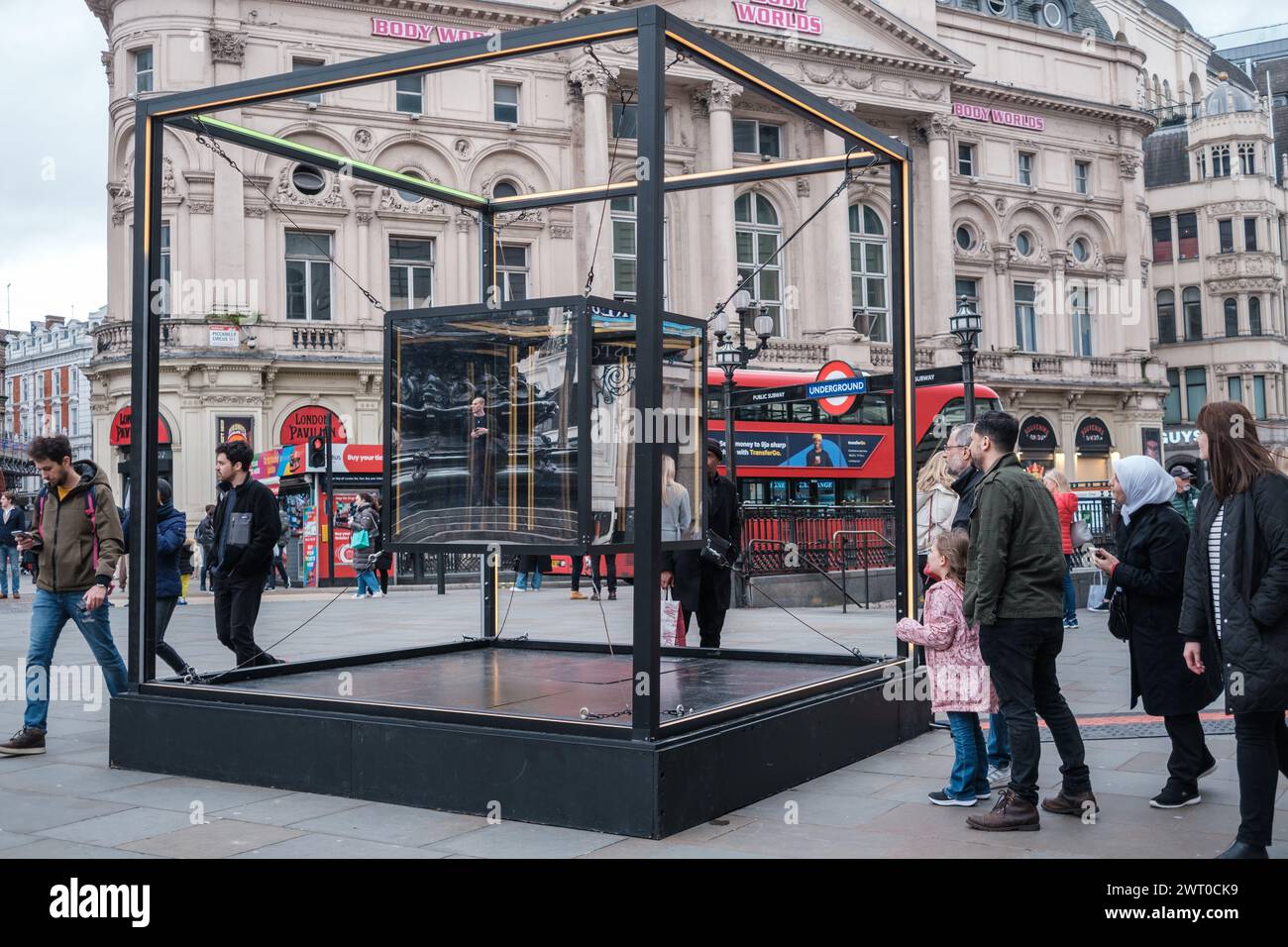 Passersby look at metal framework cube with smaller mirrored cube ...