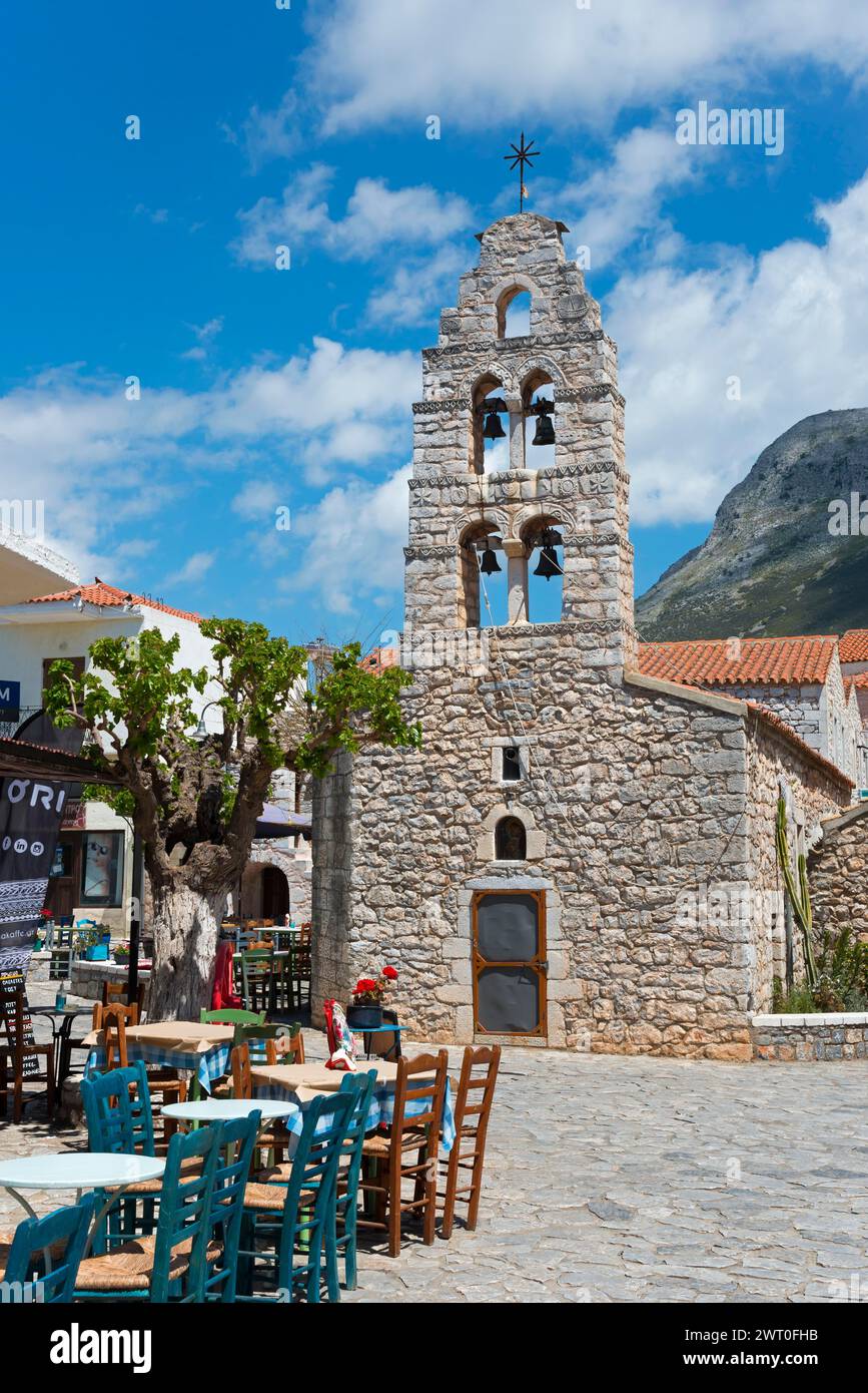 Traditional stone church with bell tower next to a cafe with terrace ...