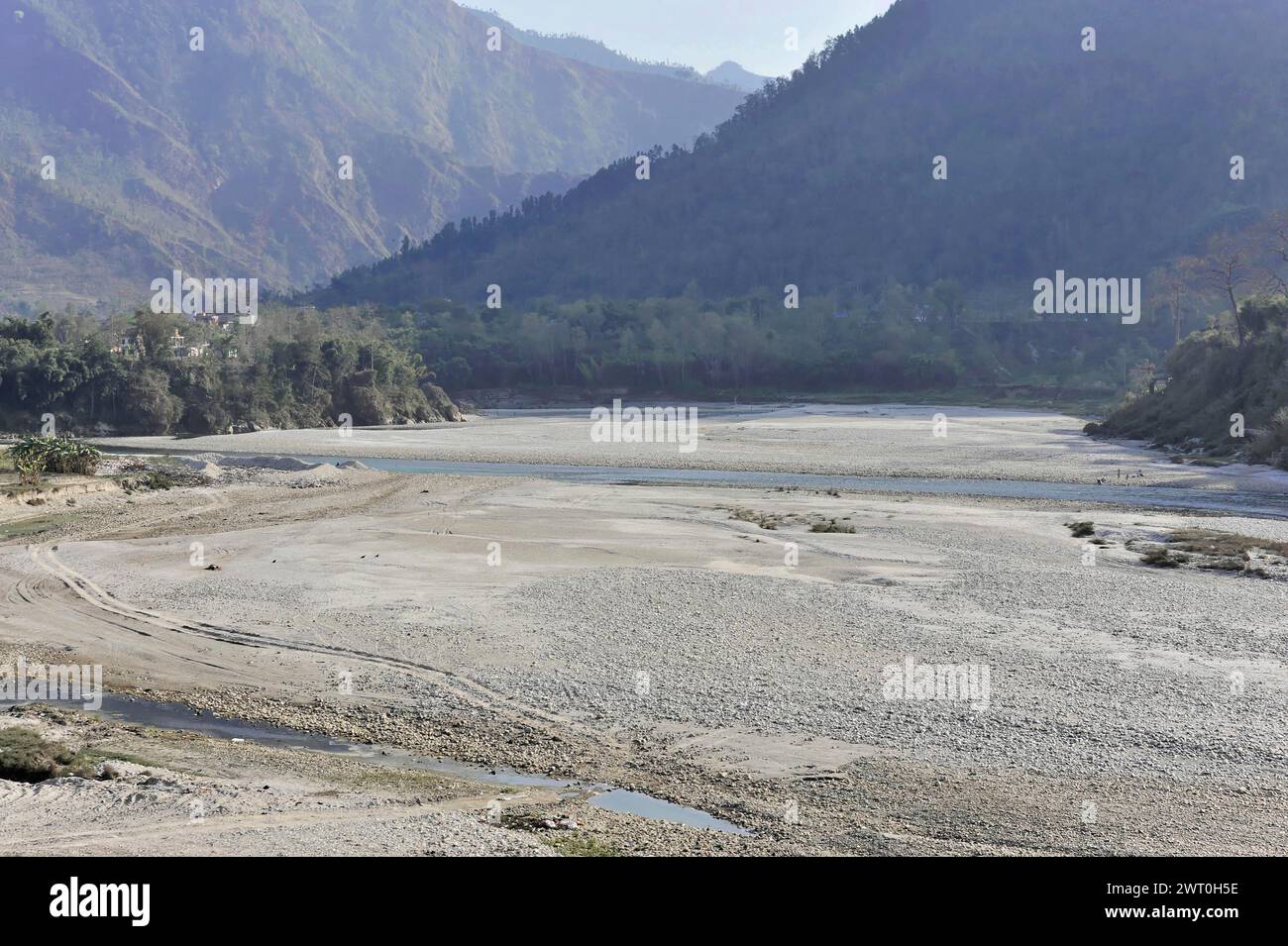 Flat river landscape surrounded by forested mountains under a clear sky ...