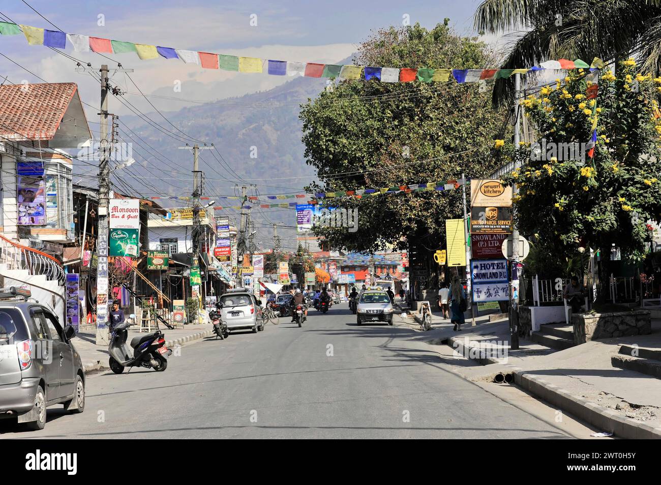 Busy street in a Nepalese town with shops and fluttering prayer flags ...