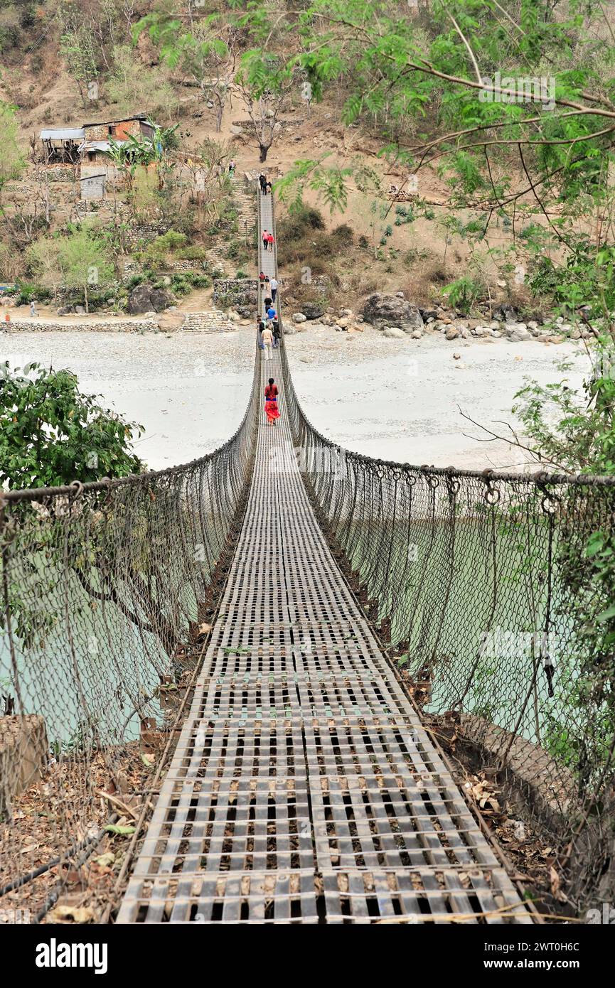 People crossing a suspension bridge over a wide river, impressions of ...