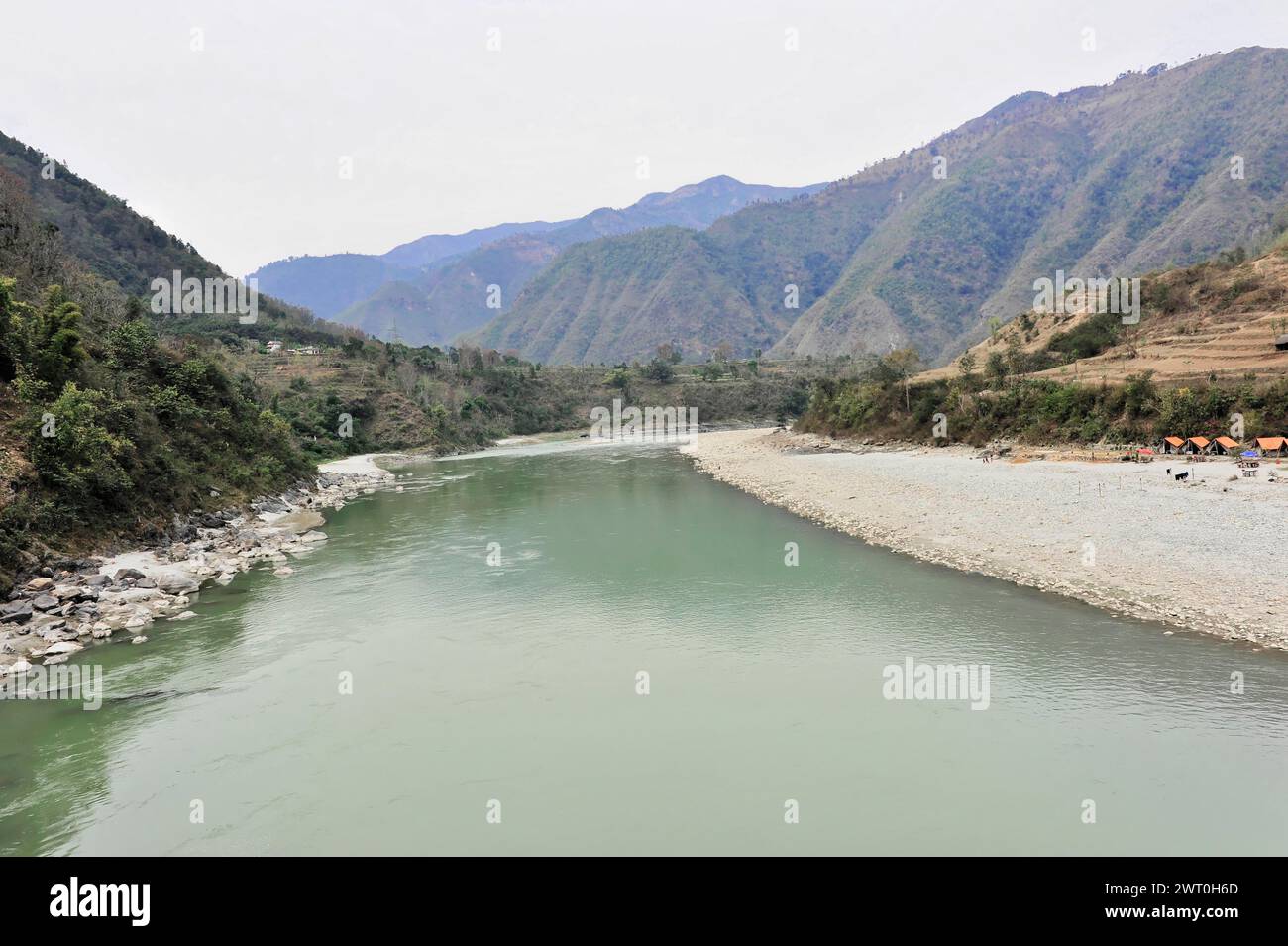 A calm river flows through a valley surrounded by mountains and green ...