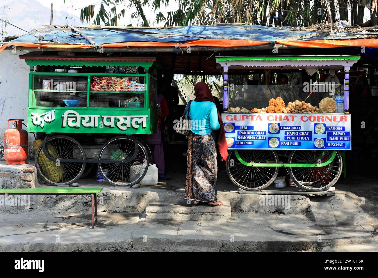 Woman standing next to a green street food stall labelled Gupta Chat ...