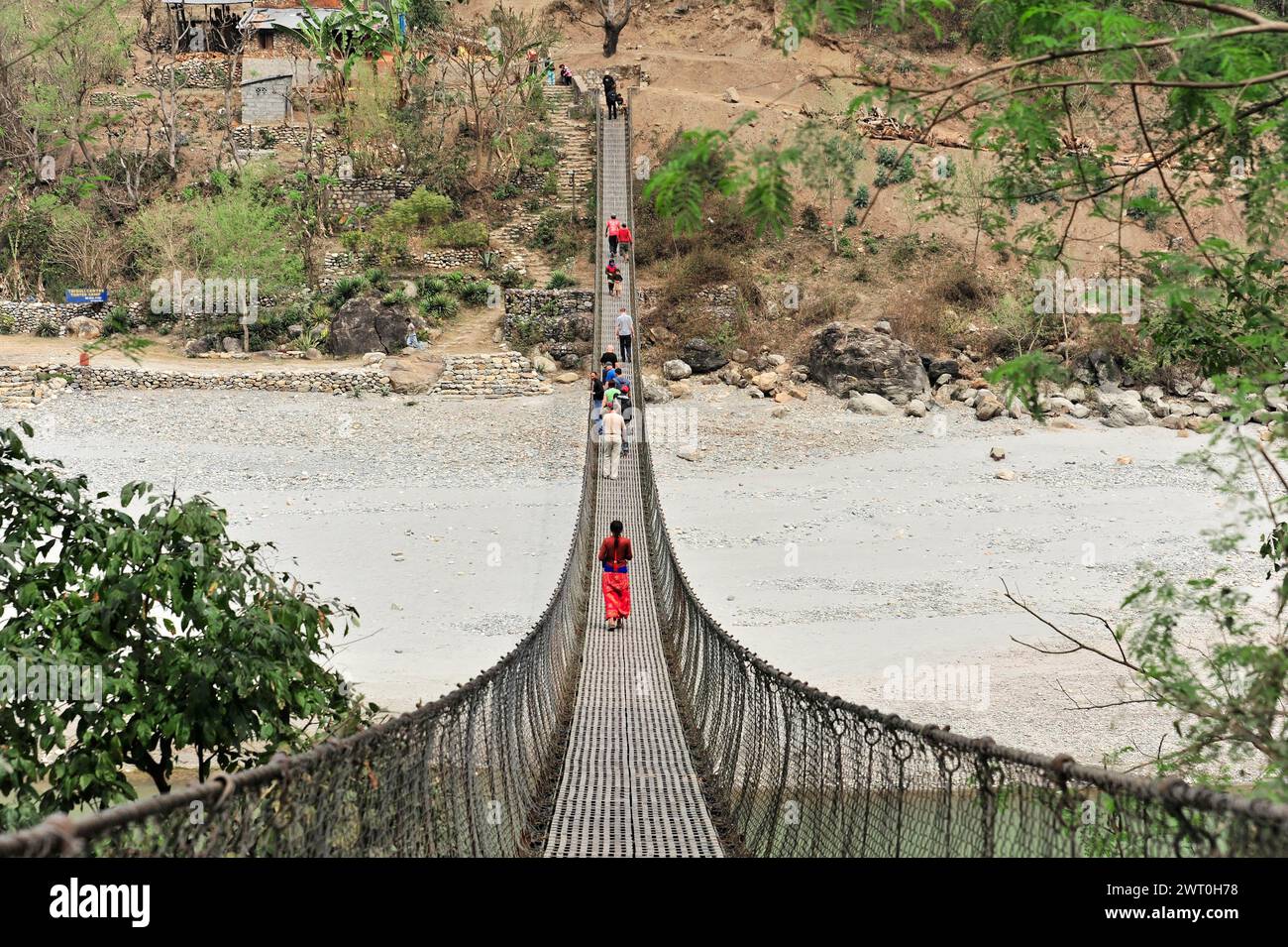 People crossing a suspension bridge over a river surrounded by green ...