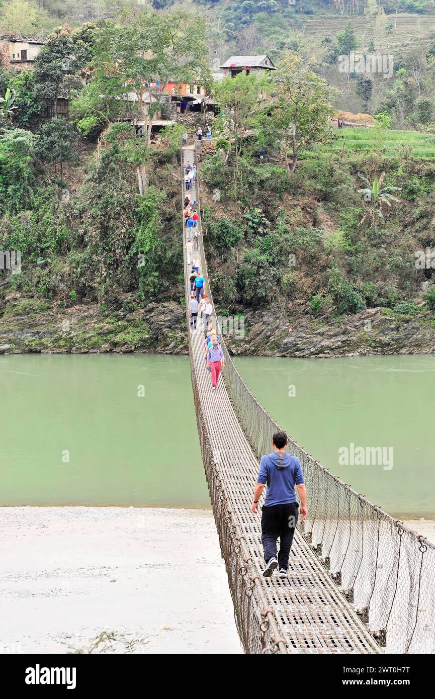 People on a suspension bridge crossing a quiet river with a view of ...