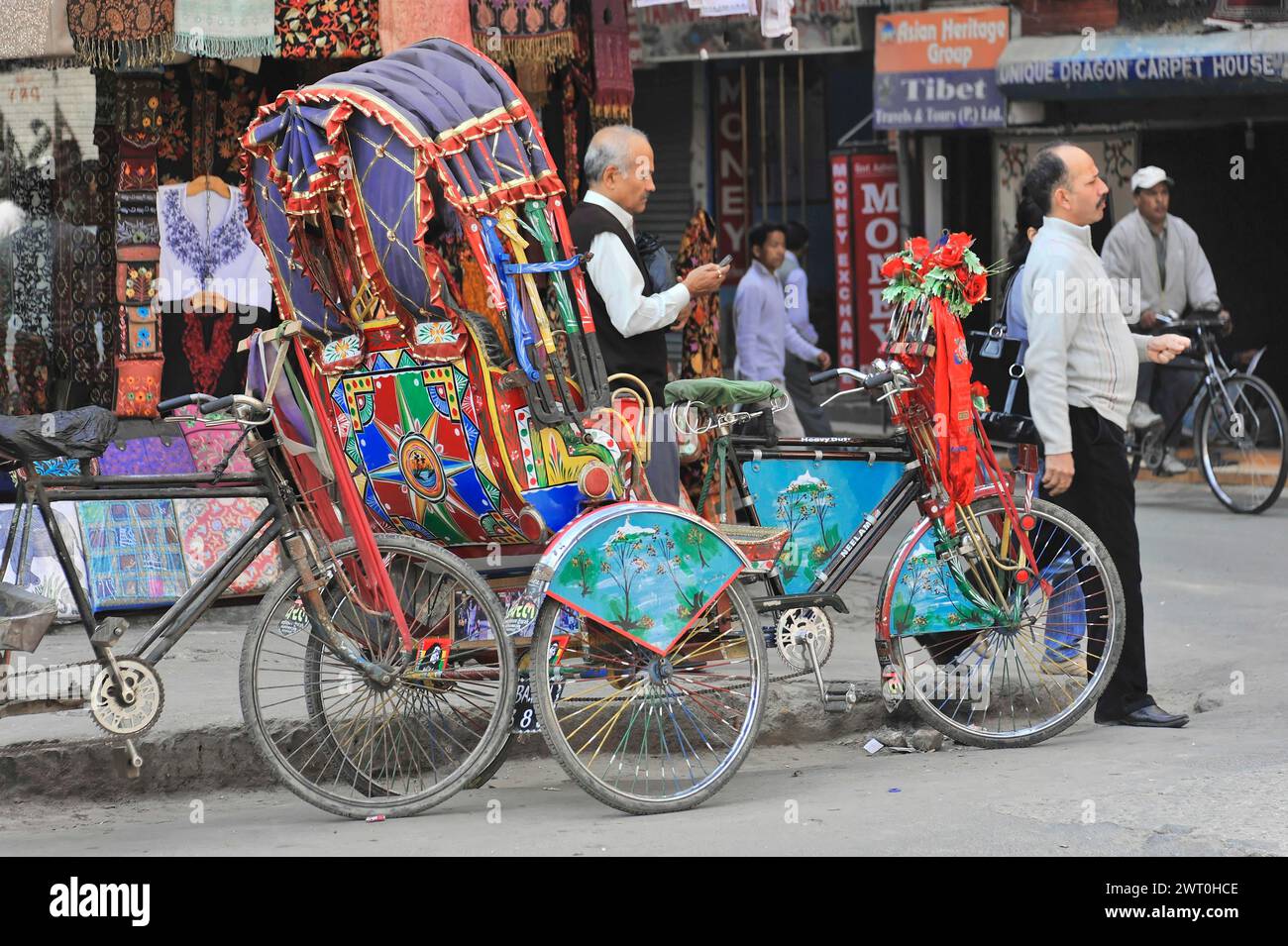 People walk past colourful parked rickshaws in front of a shop ...