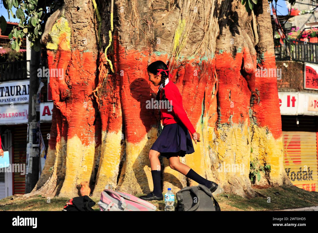 A girl in a red school uniform walks past a tree extensively painted ...